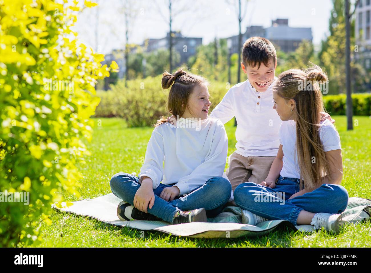 Three children have fun sitting on a green lawn in a city park Stock ...
