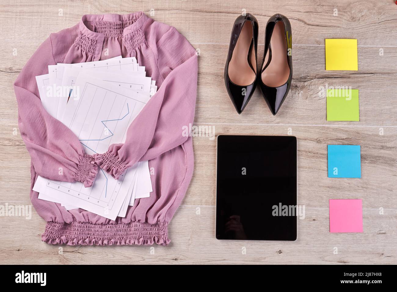 Top view flat lay pink blouse with work papers and shoes. Tablet with ...