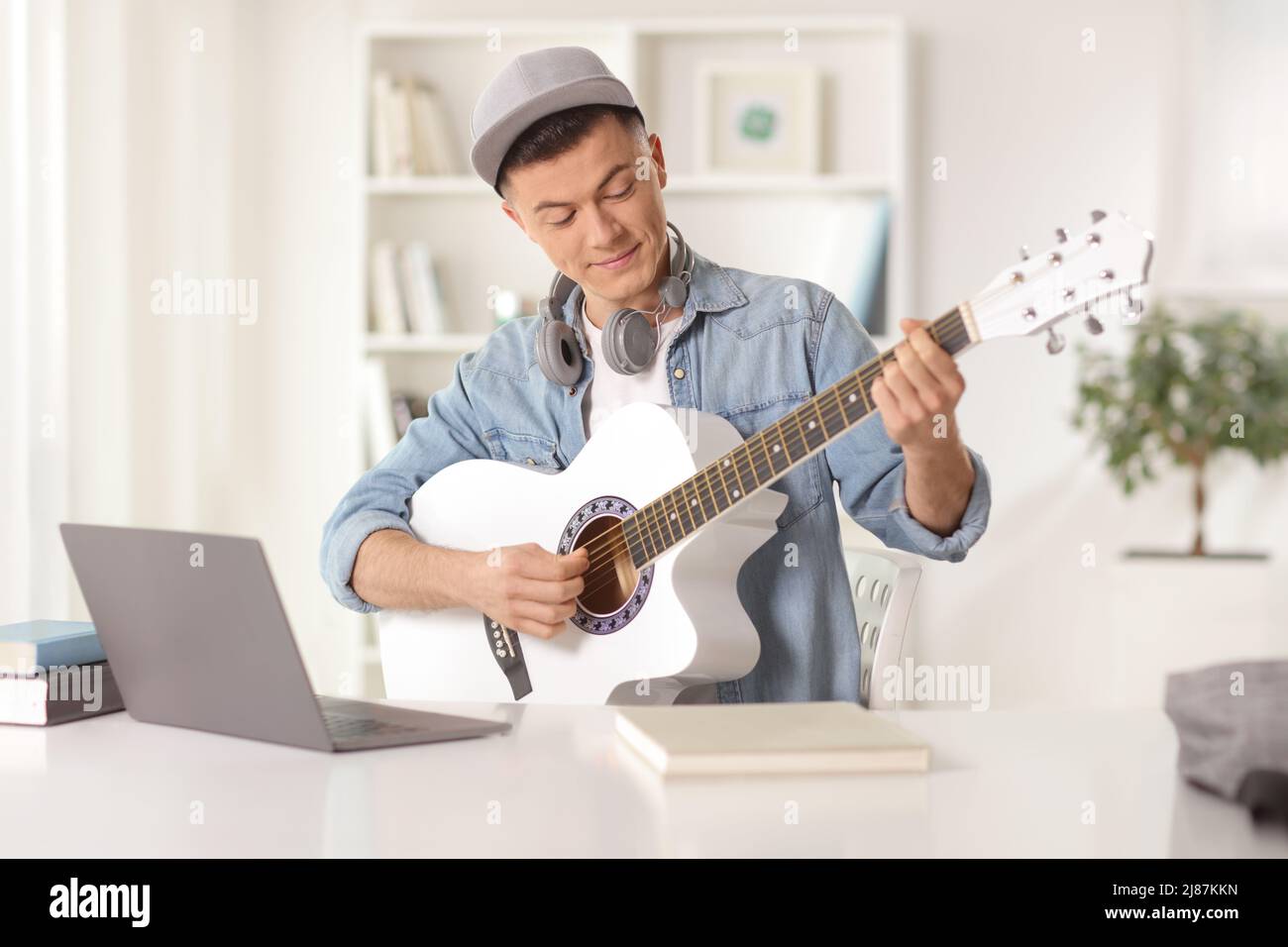 Young male musician in front of a laptop computer at home playing an ...