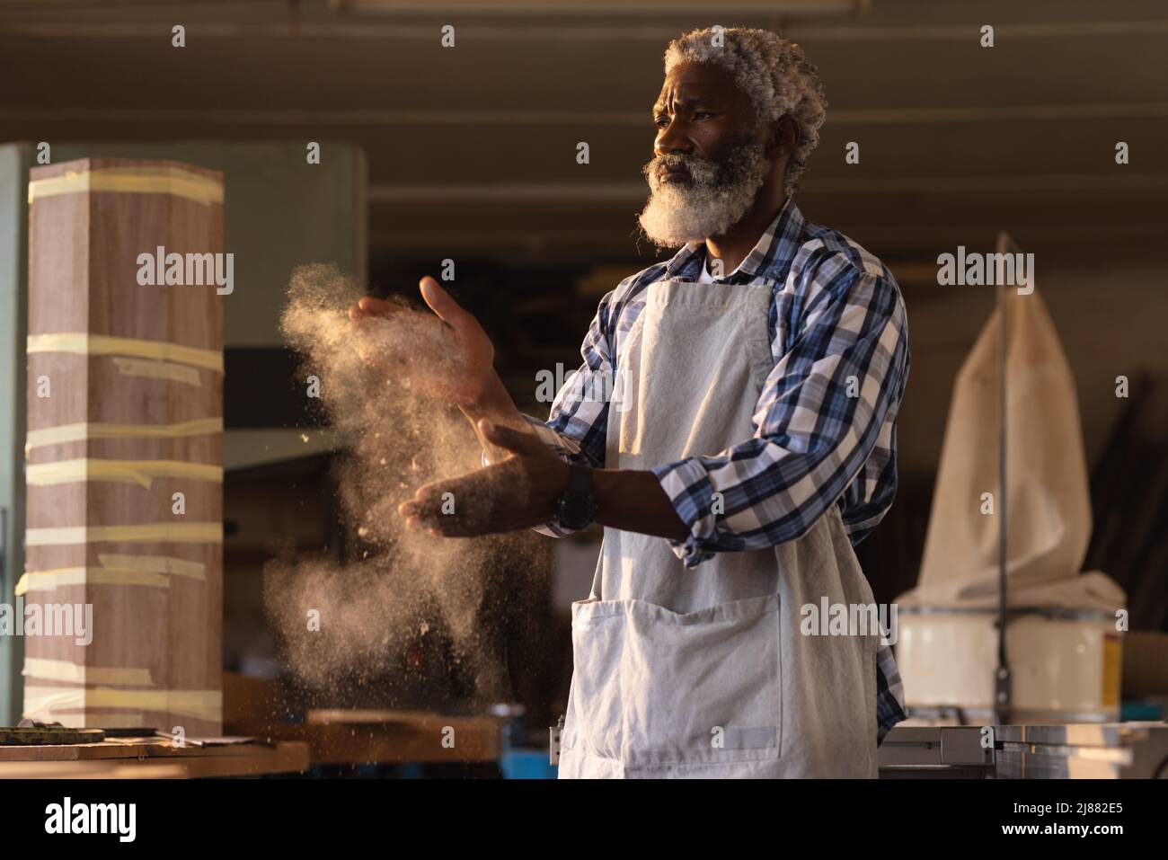 African american mature carpenter dusting sawdust on hands in workshop ...