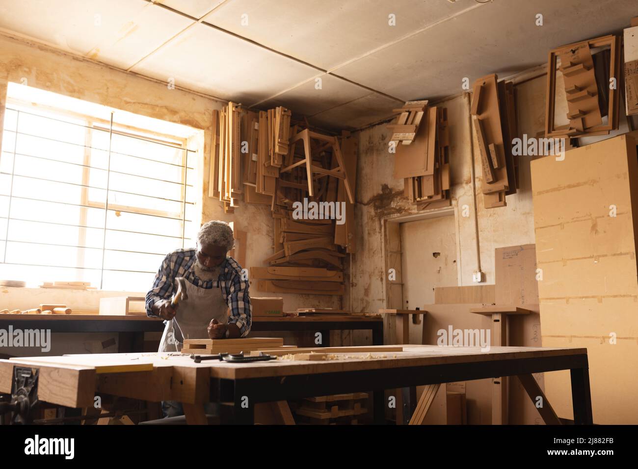 African american mature carpenter nailing plank at workbench in ...