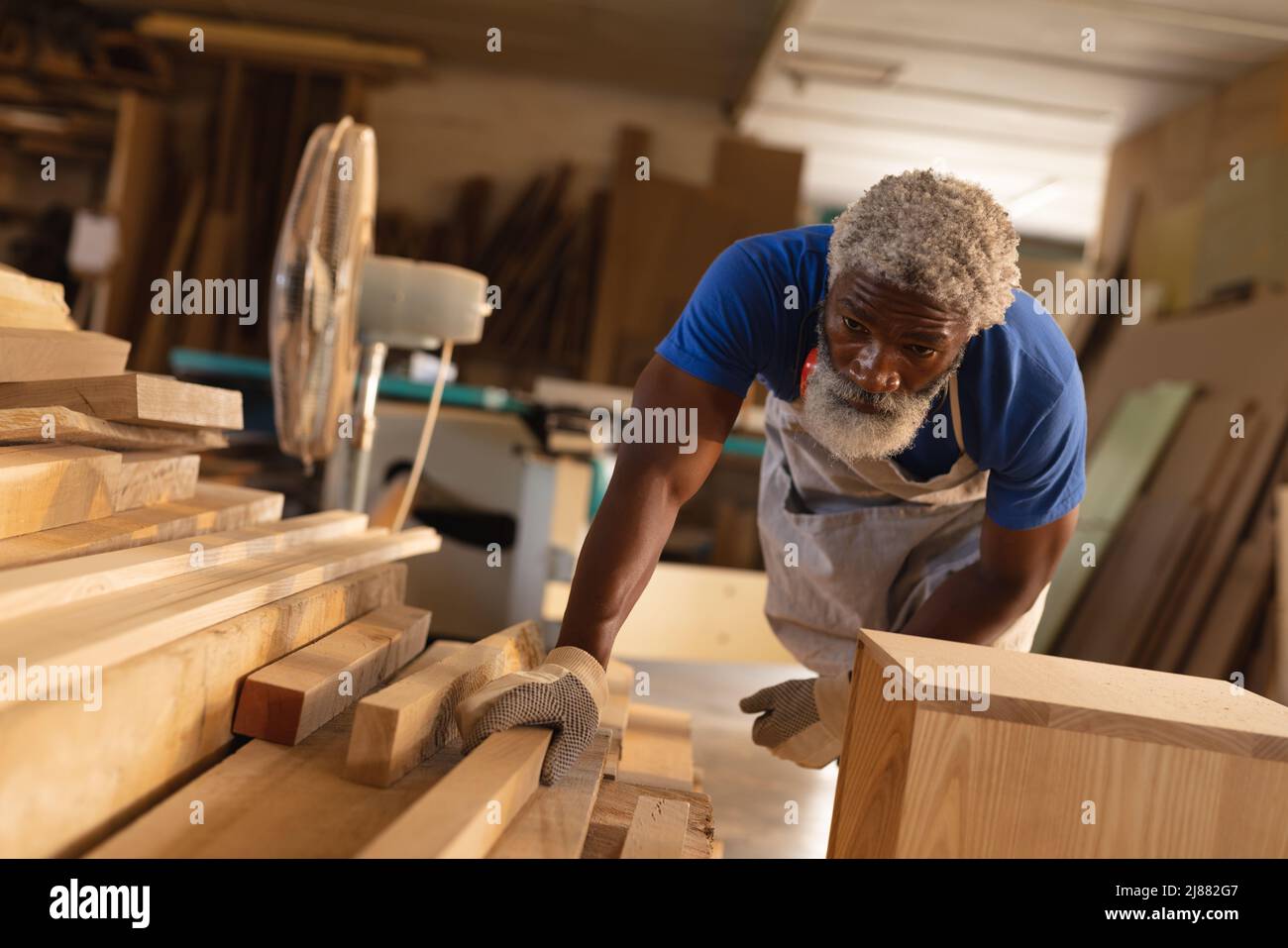 African american mature carpenter examining planks while working in ...