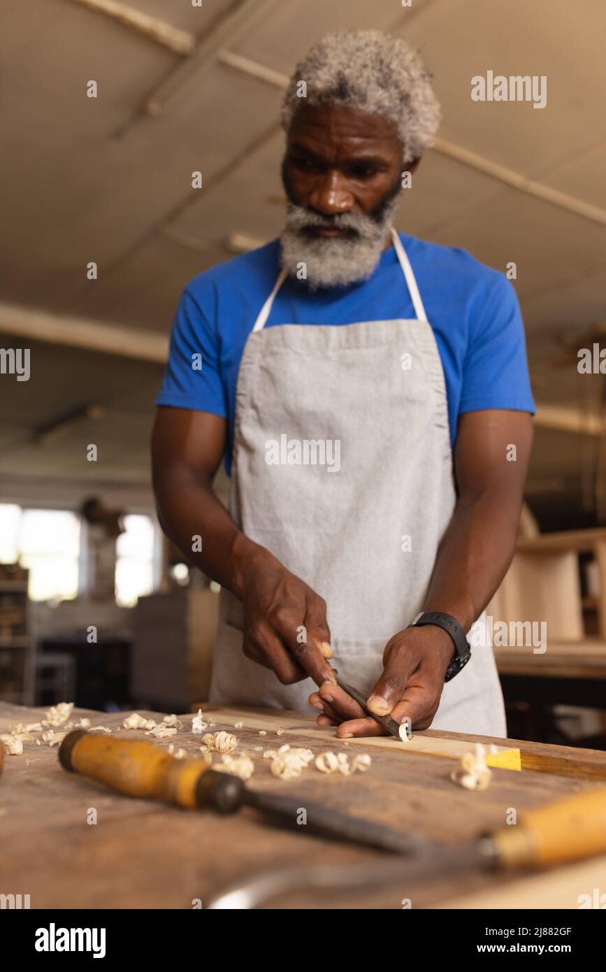 African american mature carpenter using chisel on plank at workbench in ...