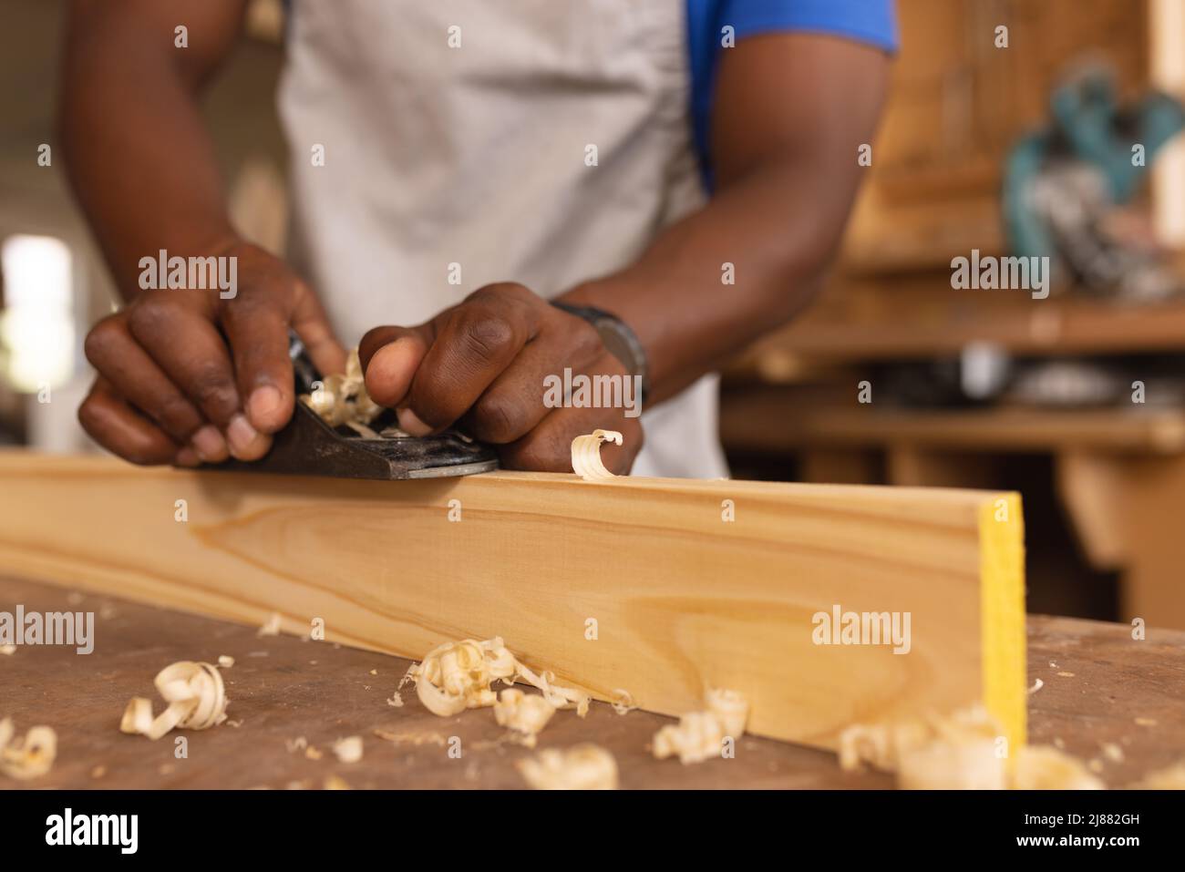 Midsection of african american mature carpenter planing plank in ...