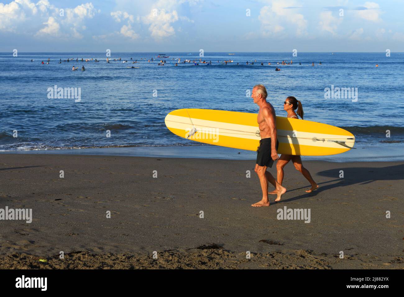 An elderly male Caucasian man carrying a yellow longboard at Batu ...