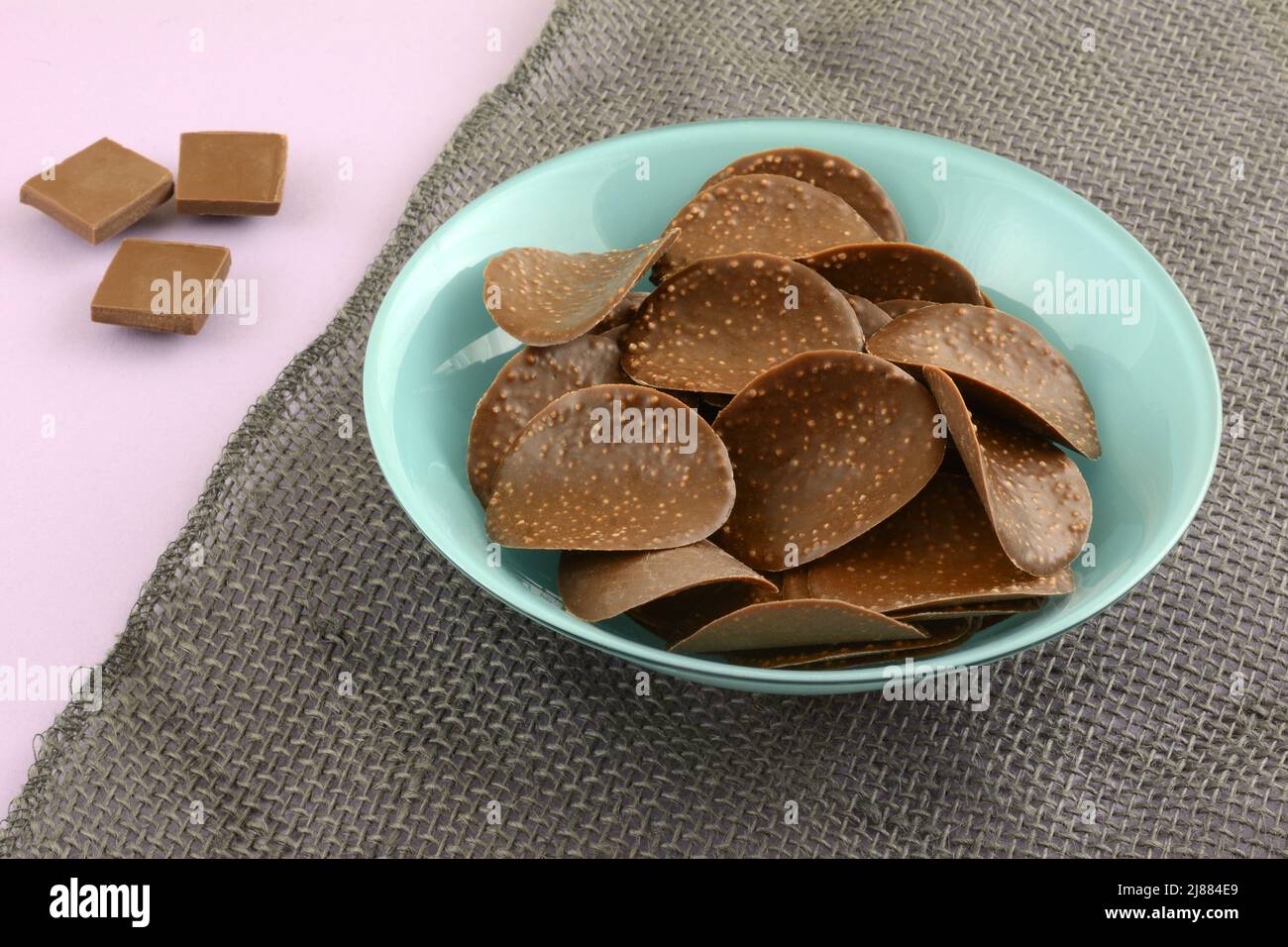 Chocolate covered chip crisps in blue snack bowl on gray burlap with ...