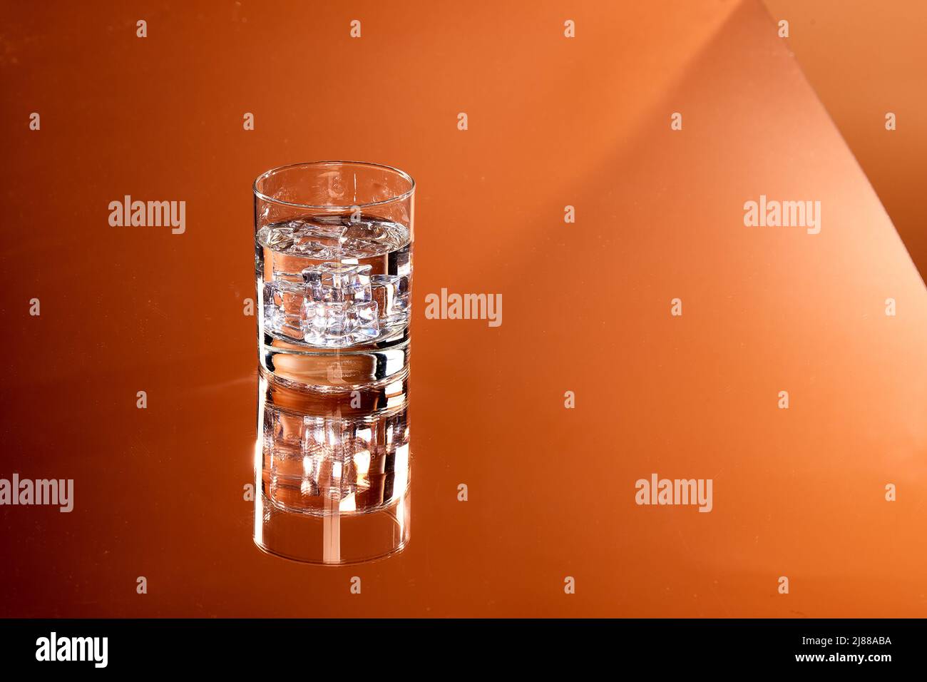Glass of water with ice cubes on orange and copper background with copy ...