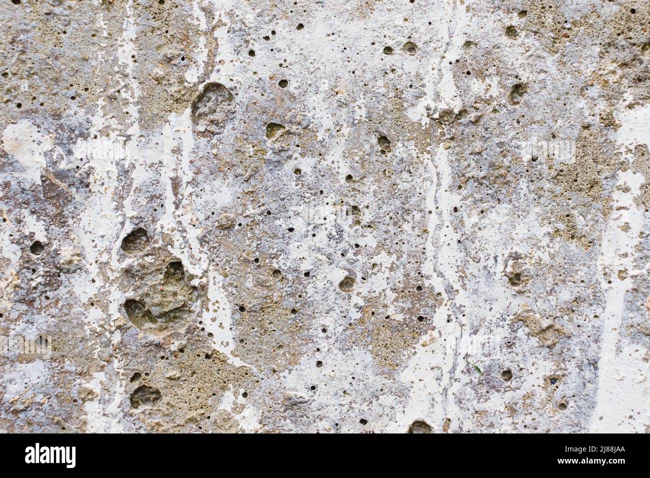 An old concrete wall with remnants of gray paint crumbling from time ...