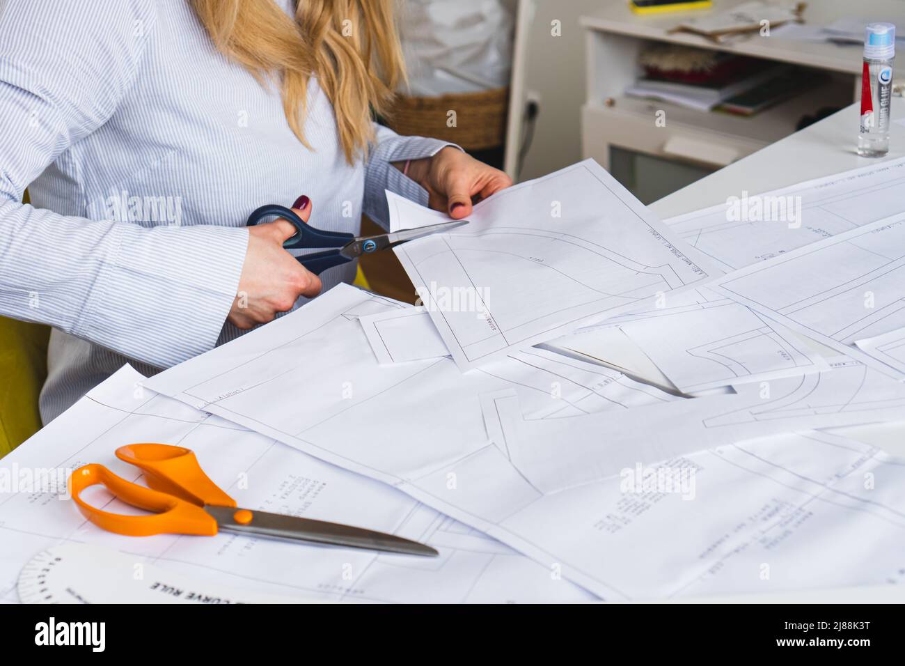 Seamstress cuts papper patterns for dress with scissors. Design ...