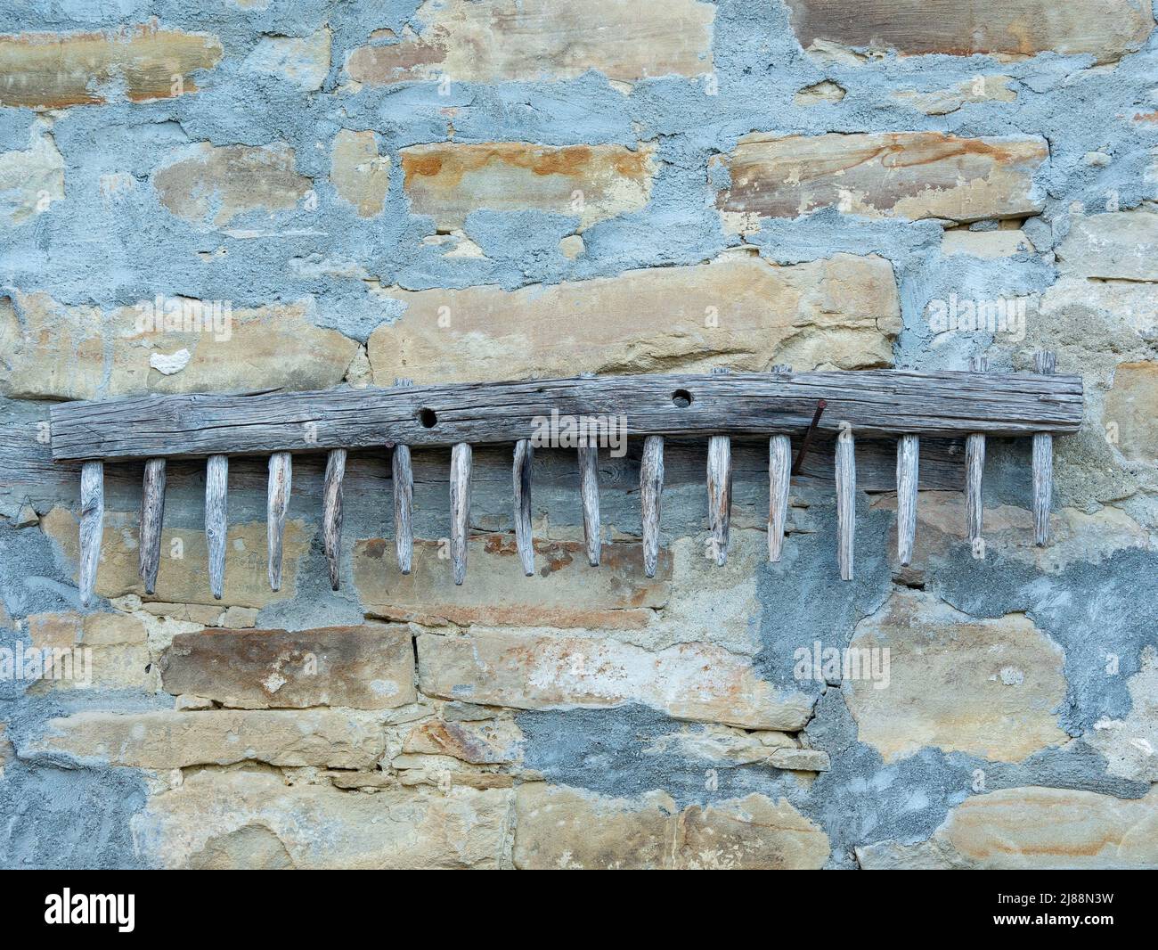 old wooden rake hanging on a stone wall of a country house example of ...