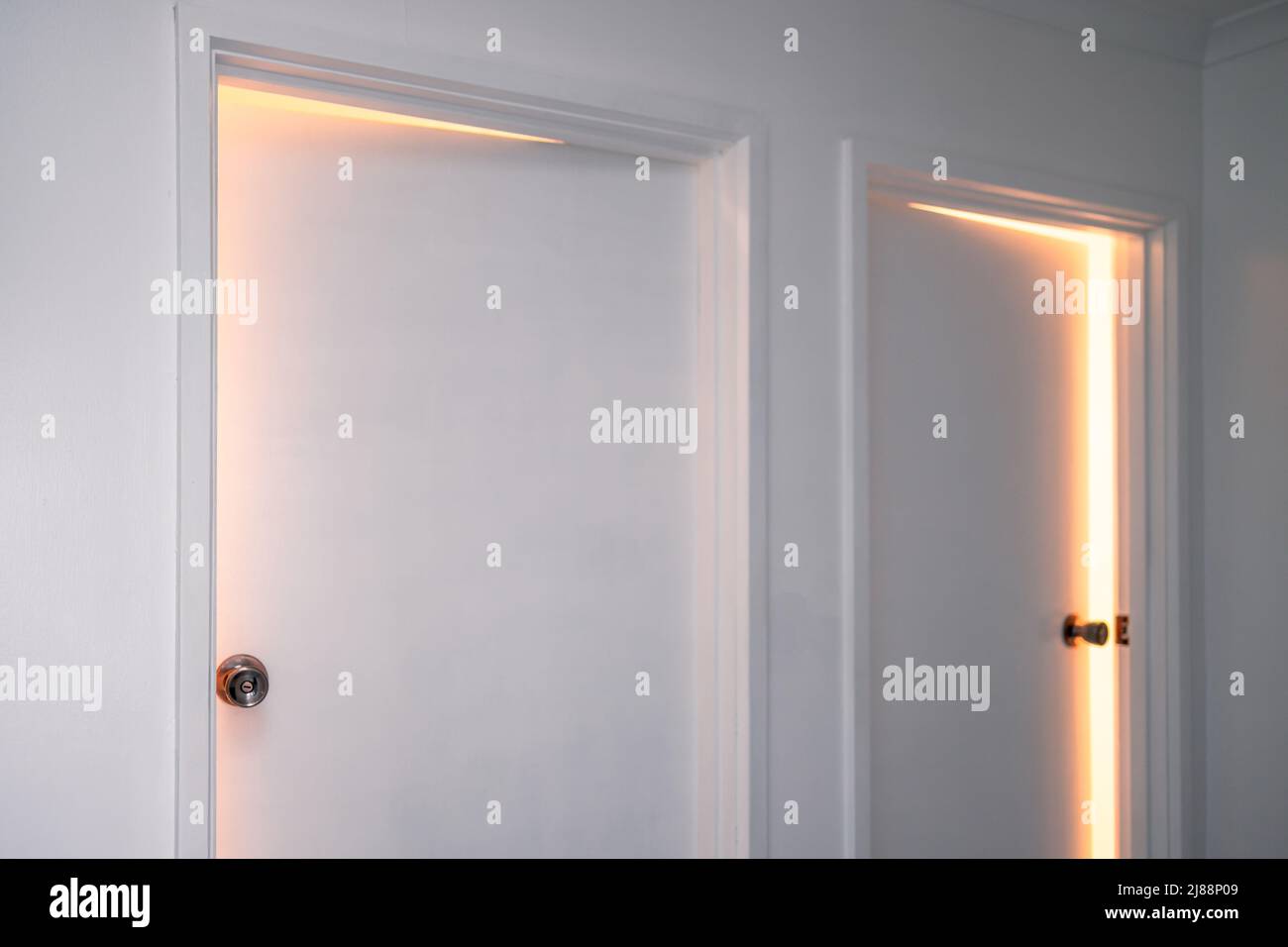 interior corridor with two white doors left ajar and light shining from ...