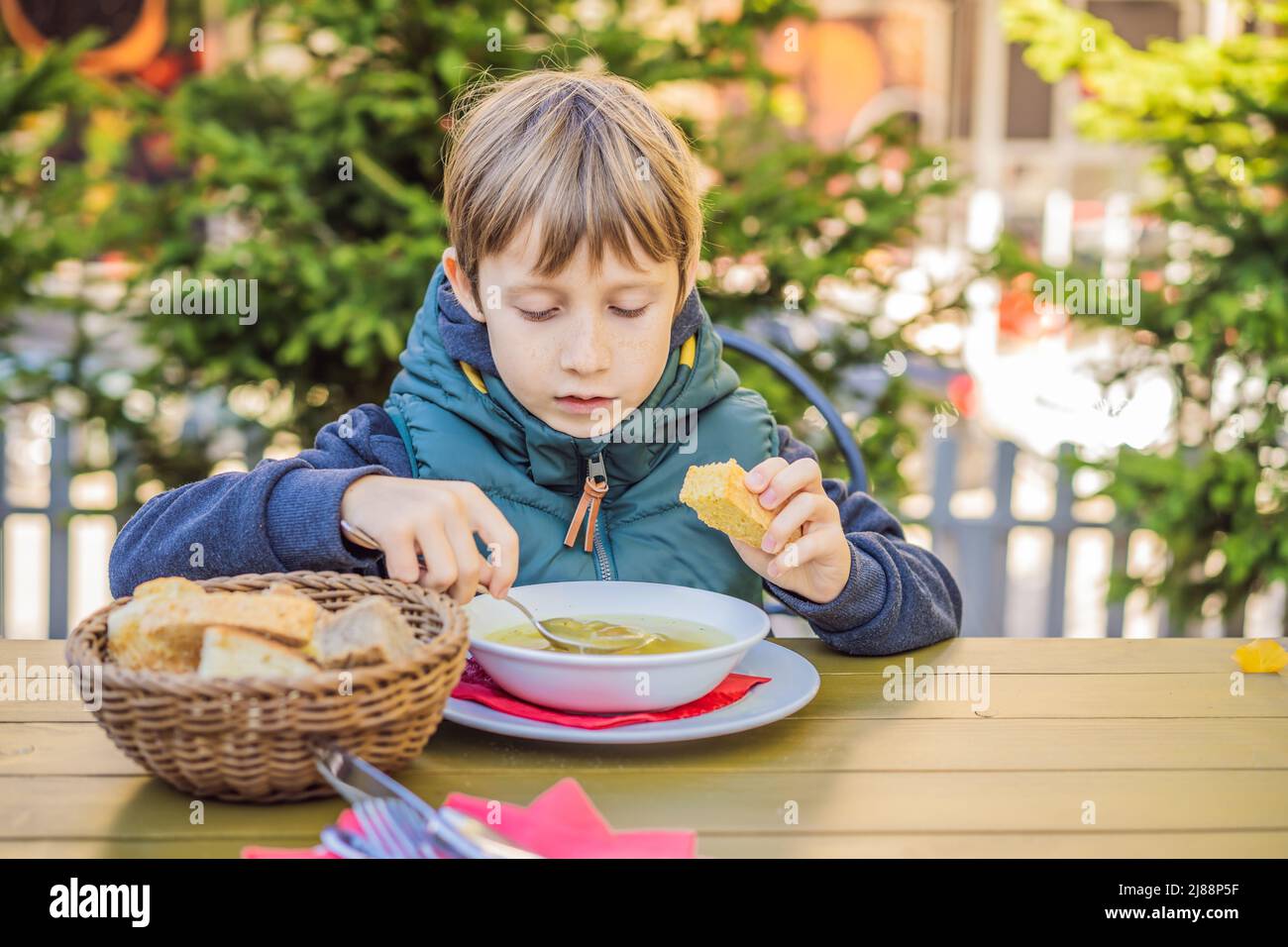 Adorable little school boy eating vegetable soup outdoor. Blond child ...