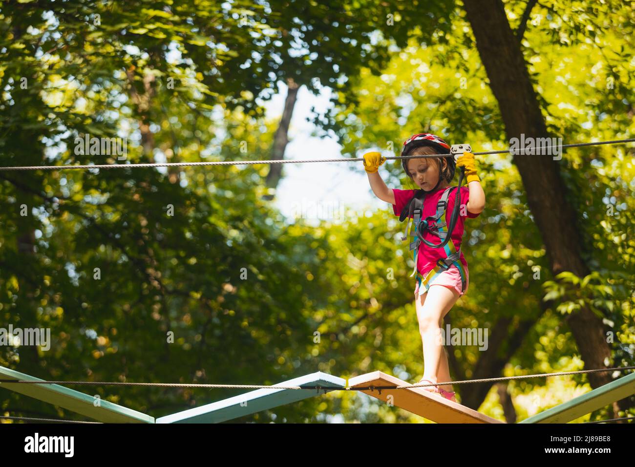 The concentrated girl carefully overcomes obstacles in the rope park ...