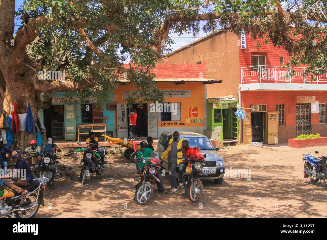 Group of men on motorbikes in front of small shops in Kenyan village ...