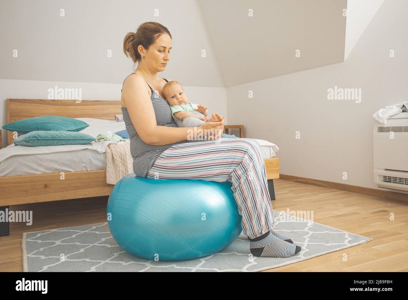 Mother holding and rocking baby sitting on fitball Stock Photo - Alamy
