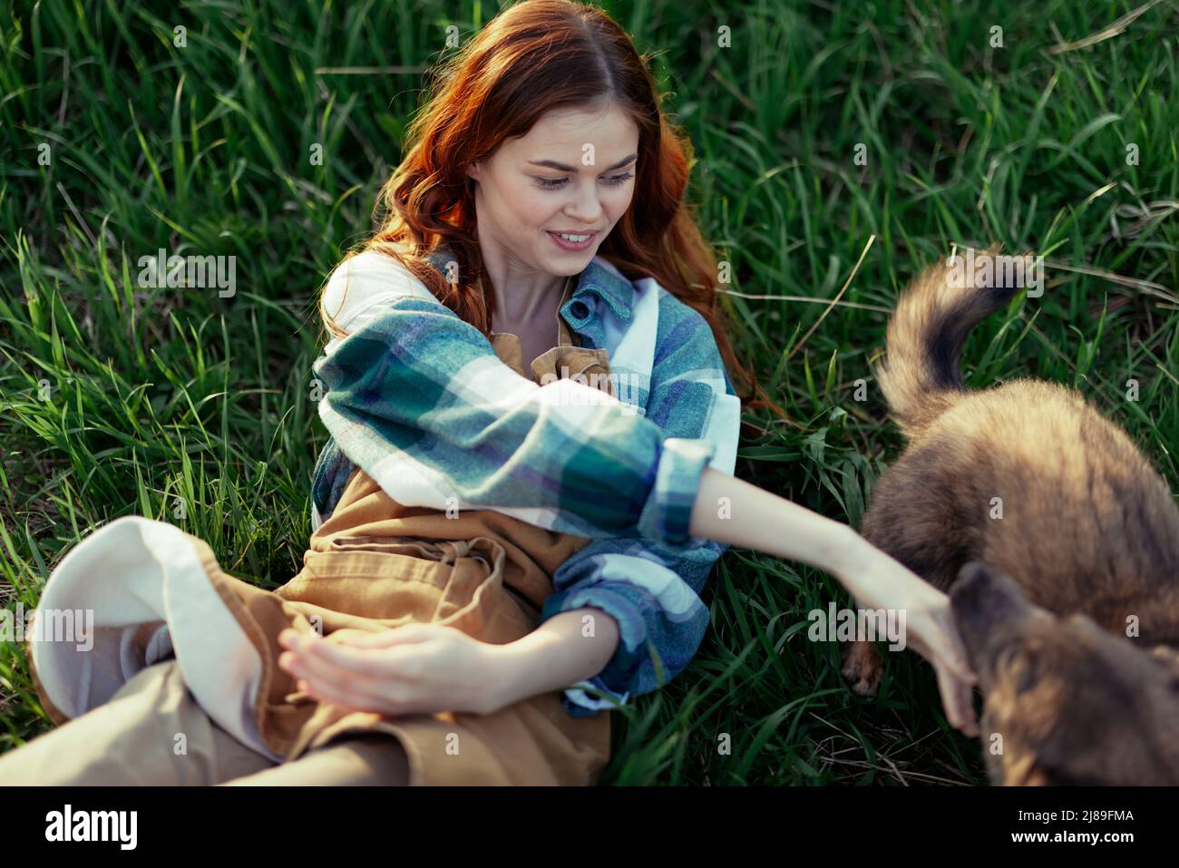 Woman lying on the grass smiling playing and cuddling her dog in nature ...