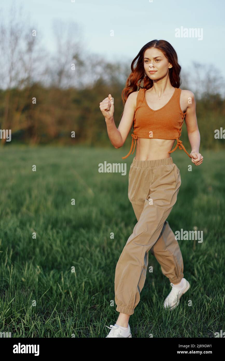 A woman of athletic build runs through the park on the green grass with ...
