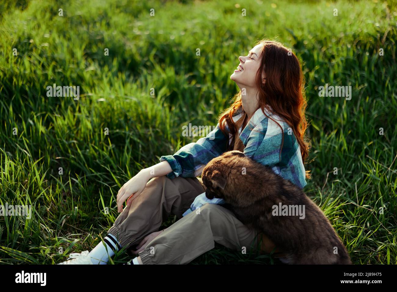 Woman lying on the grass smiling playing and cuddling her dog in nature ...
