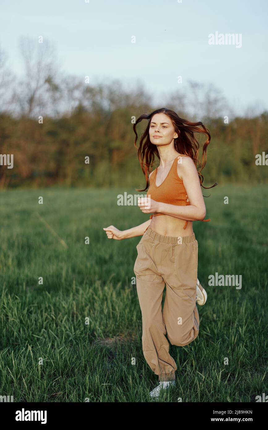 A woman of athletic build runs through the park on the green grass with ...