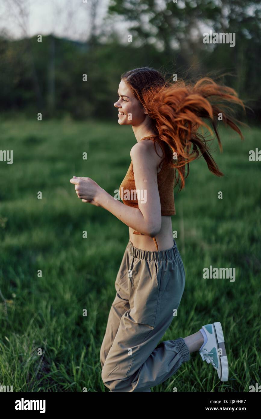 An athletic woman jogs on the grass in green pants and sneakers and ...