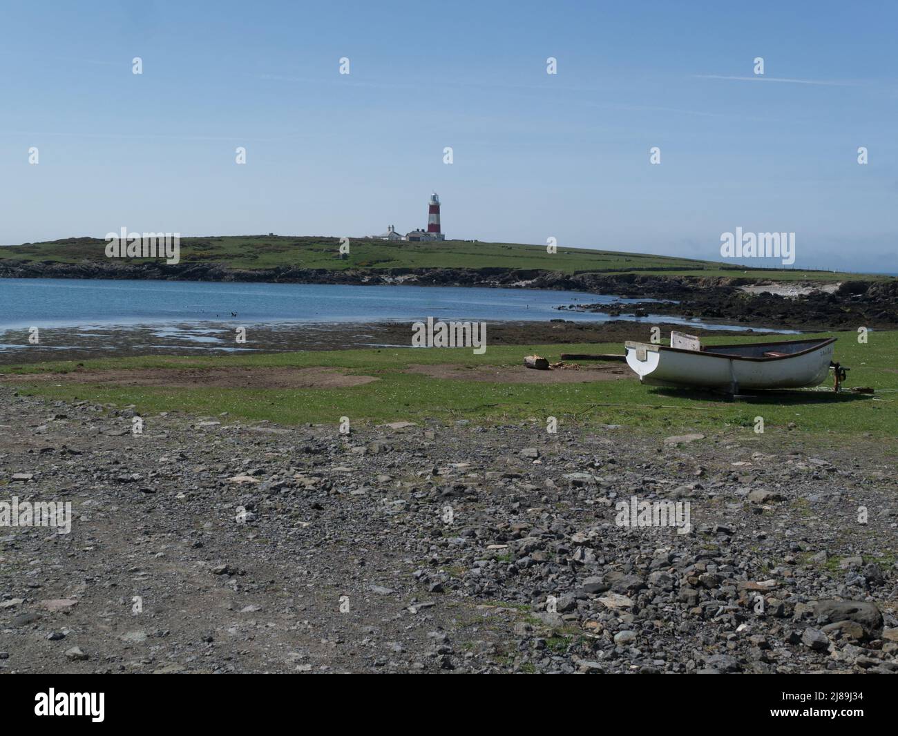 View across a moored rowing boat to lighthouse on Bardsey Island ...