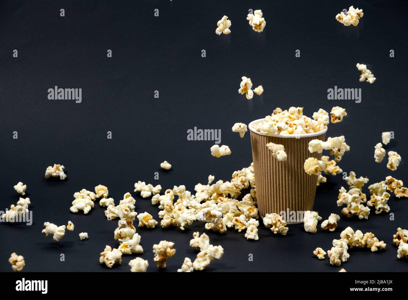 Popcorn is poured into a paper brown glass on a black background with ...