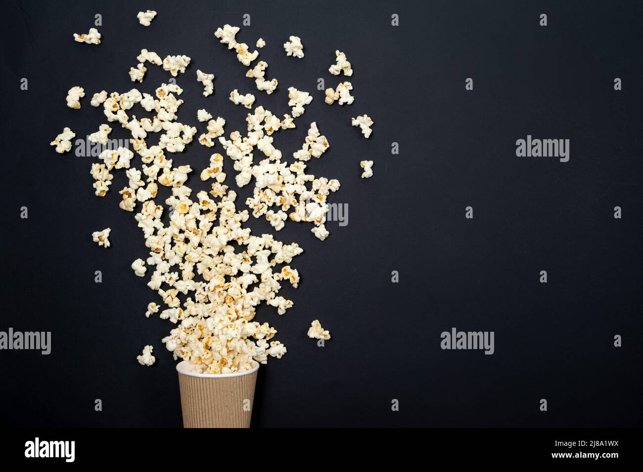 Popcorn spills out of the glass on a black background, viewed from ...