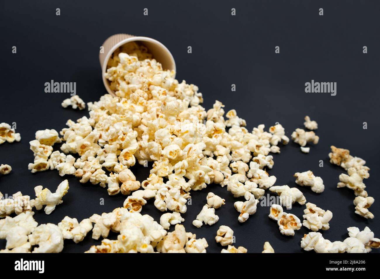 Popcorn spills out of a brown paper cup on a black background close-up ...