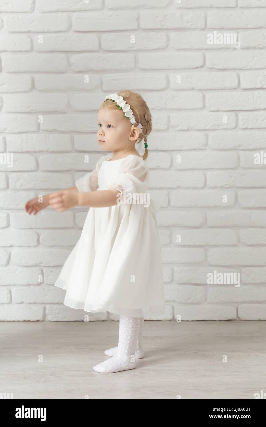 Baby child with hearing aids and cochlear implants on white brick wall ...