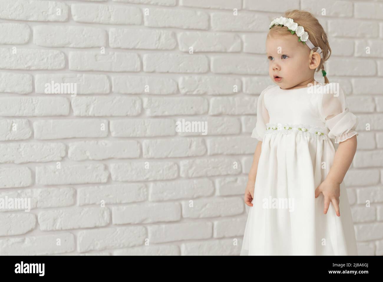 Baby child with hearing aids and cochlear implants on white brick wall ...