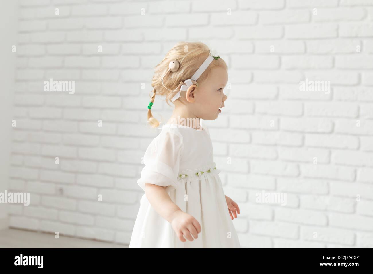 Baby child with hearing aids and cochlear implants on white brick wall ...
