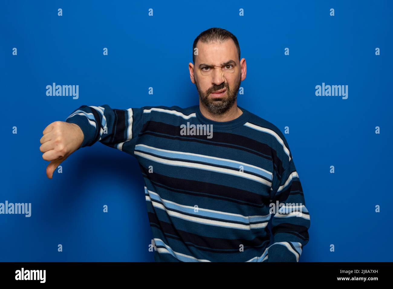 Latin man wearing striped sweater standing over isolated blue ...