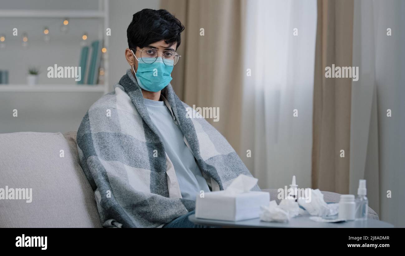 Sick arab man in medical face protective mask sitting on couch at home ...