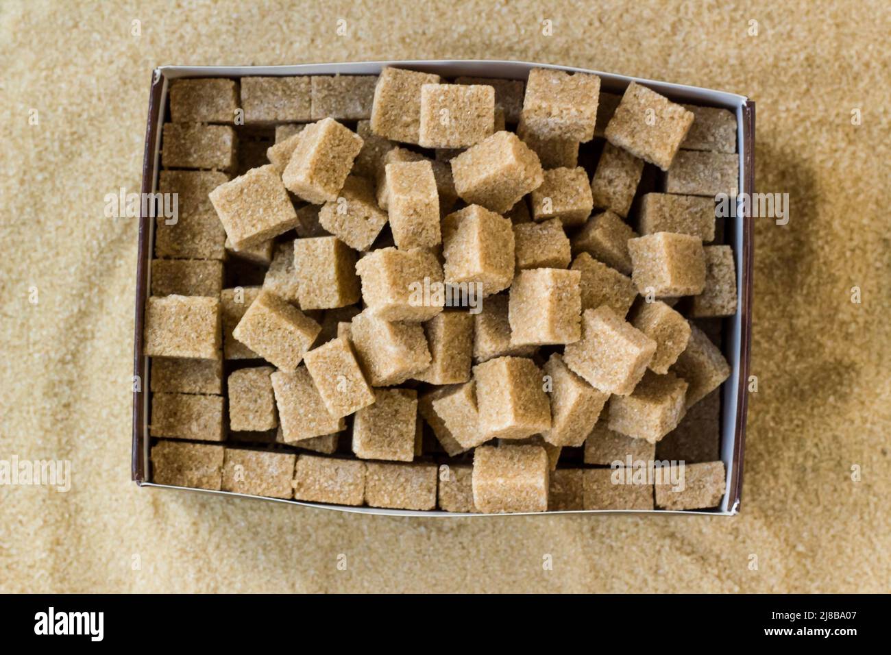 Natural, brown sugar cubes,in a cardboard box on brown,granulated sugar ...