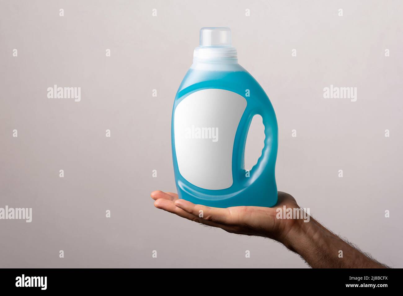 Cloth detergent liquid bottle at male hand in front of light gray ...