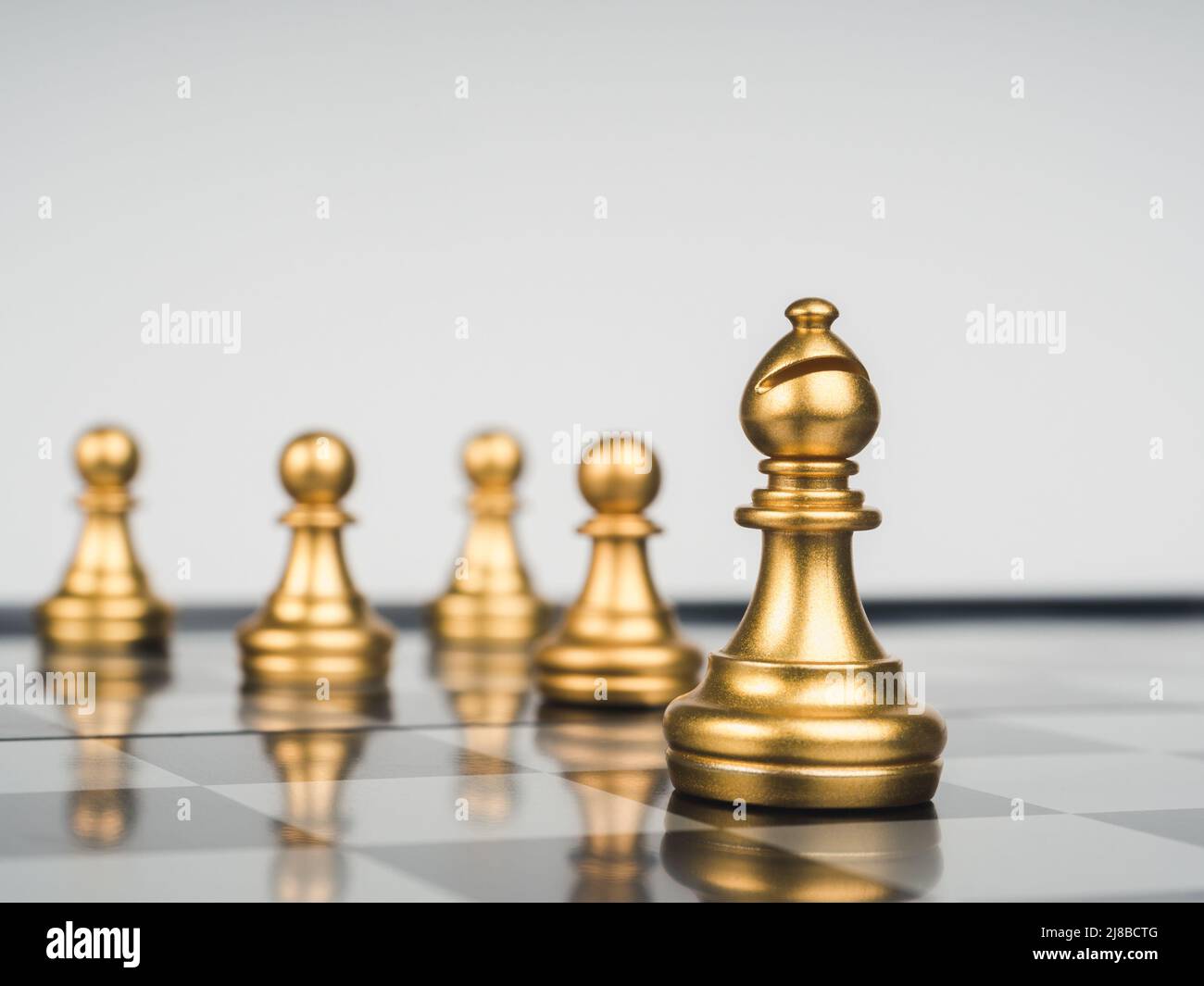 The golden bishop chess piece in front of gold pawns on chess board ...