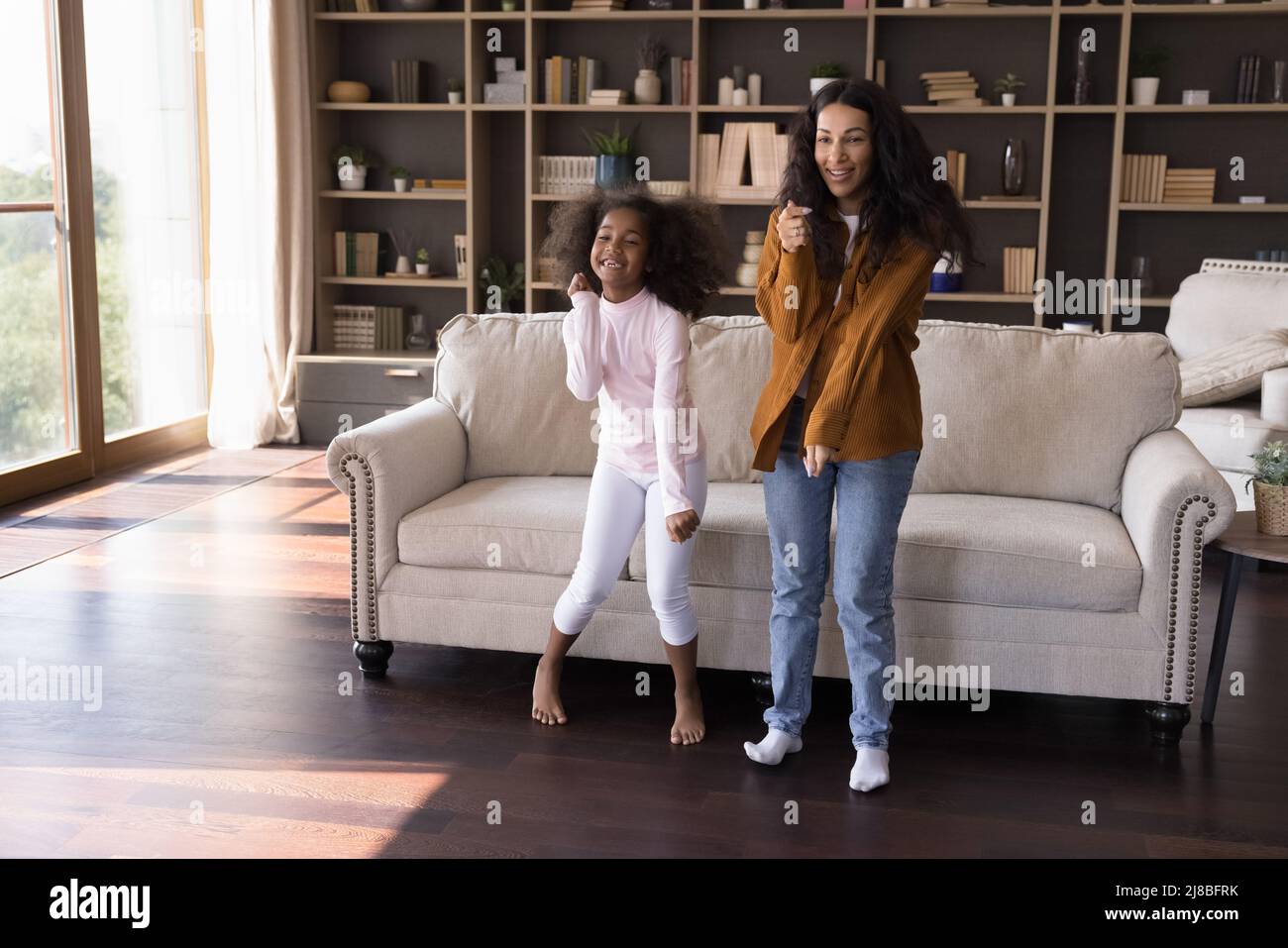 Cheerful African girl and mother dancing in modern living room Stock ...