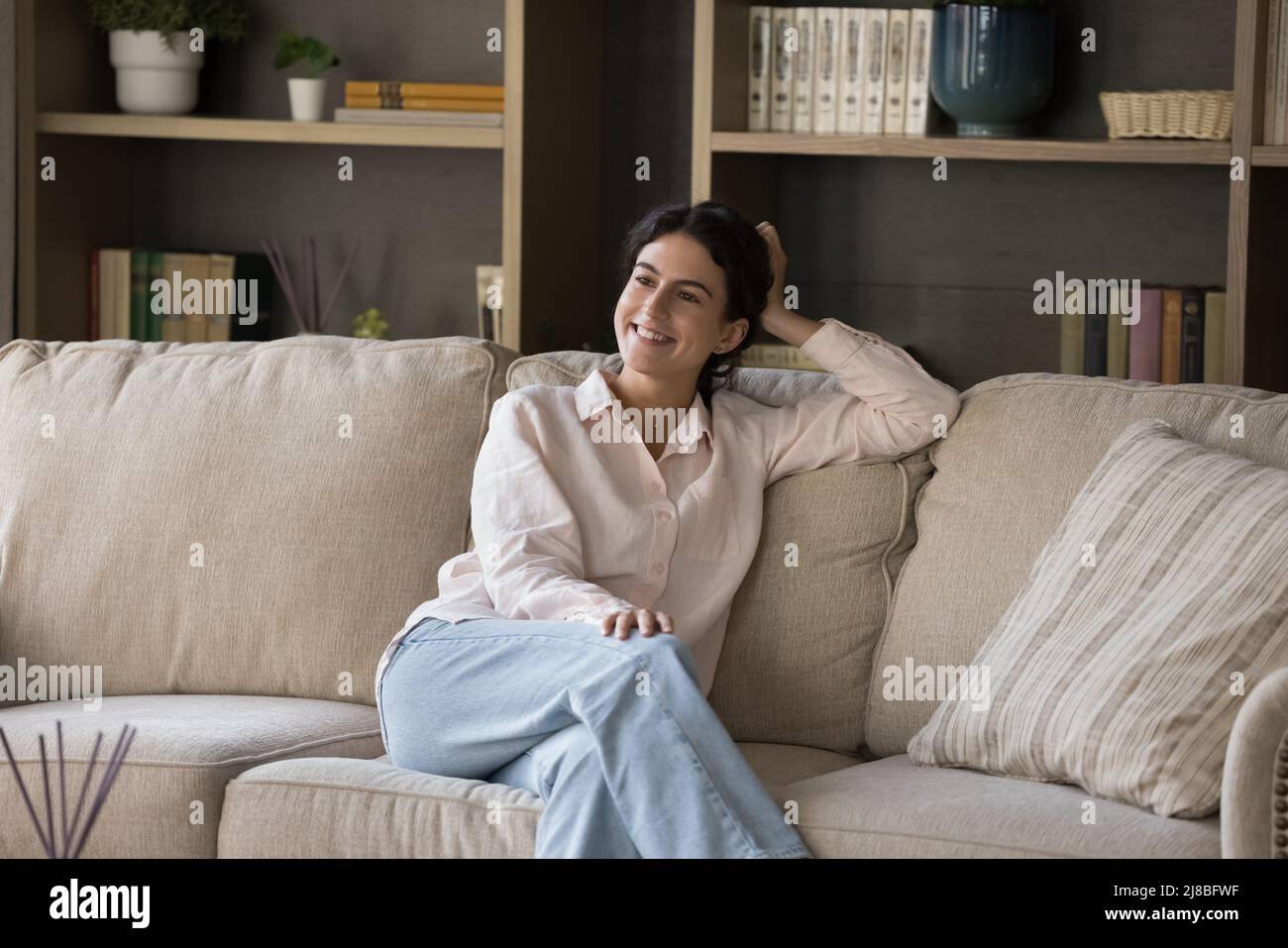 Dreamy woman relaxing on sofa in living room staring aside Stock Photo ...
