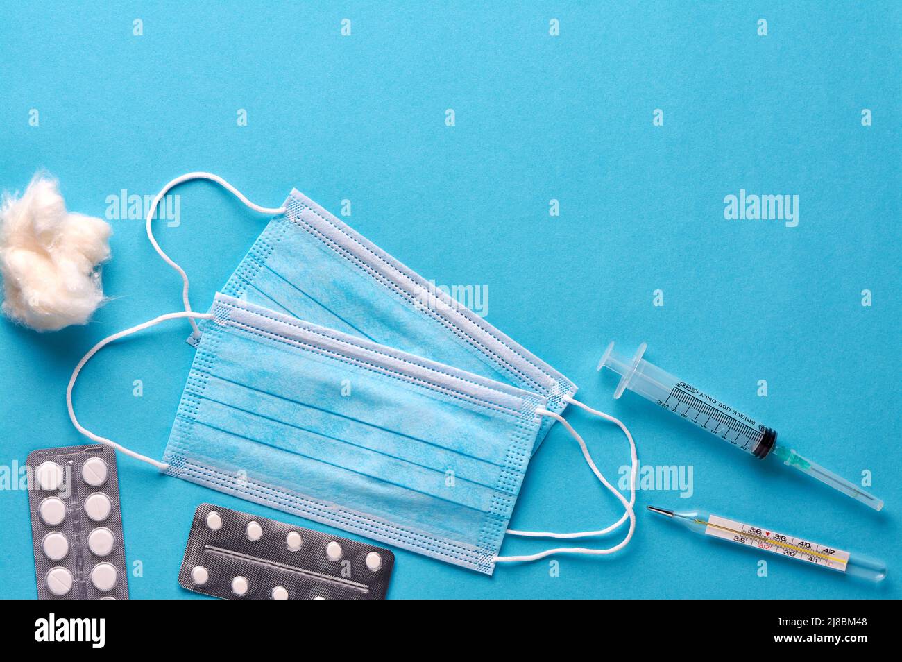 two medical masks, a syringe, a thermometer and pills lie on a blue background. flatly, copy ...