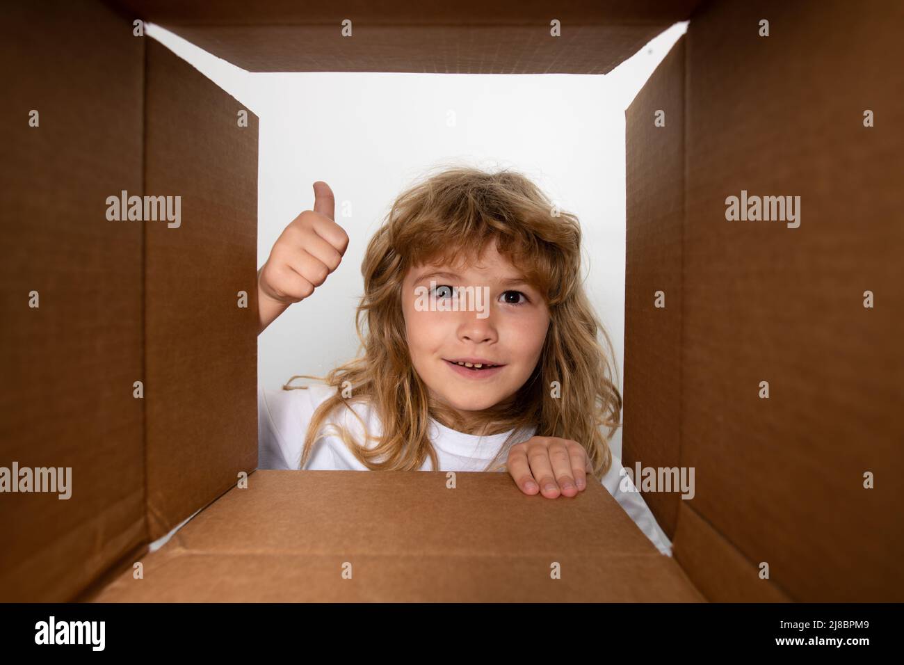 Funny child boy with thumb up is opening gift and looking inside ...