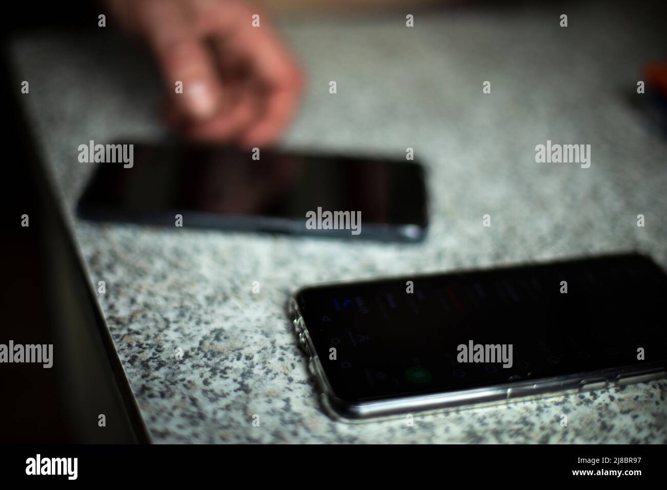 Smartphone on table. Two black phones. Hand reaches for smartphone ...