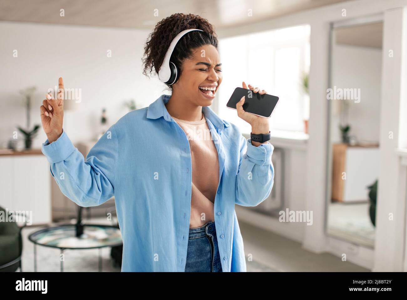 Black lady listening to music in headphones and singing Stock Photo - Alamy