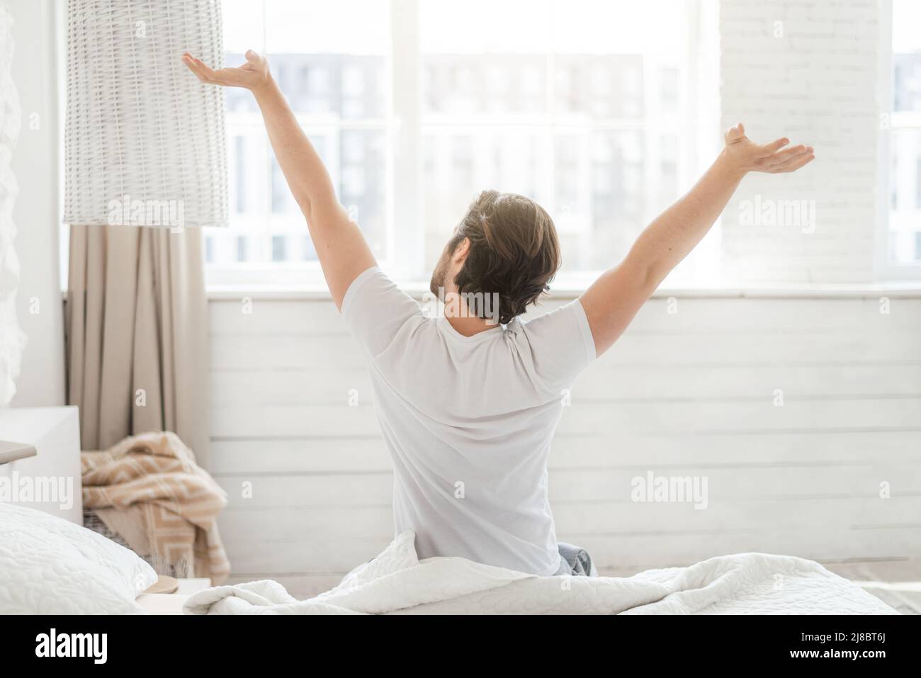 Happy millennial caucasian guy wake up and stretching body, sitting on ...