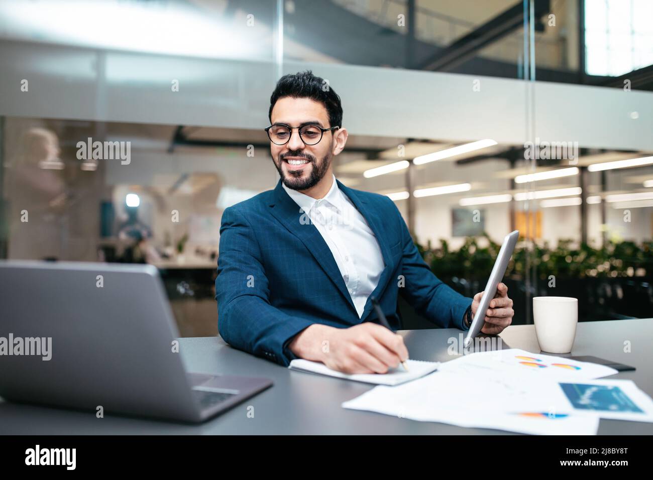 Happy attractive young islamic male with beard in glasses, suit sits at ...