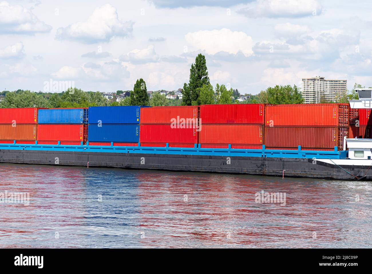 A barge carrying many containers on the Rhine in western Germany, trees ...