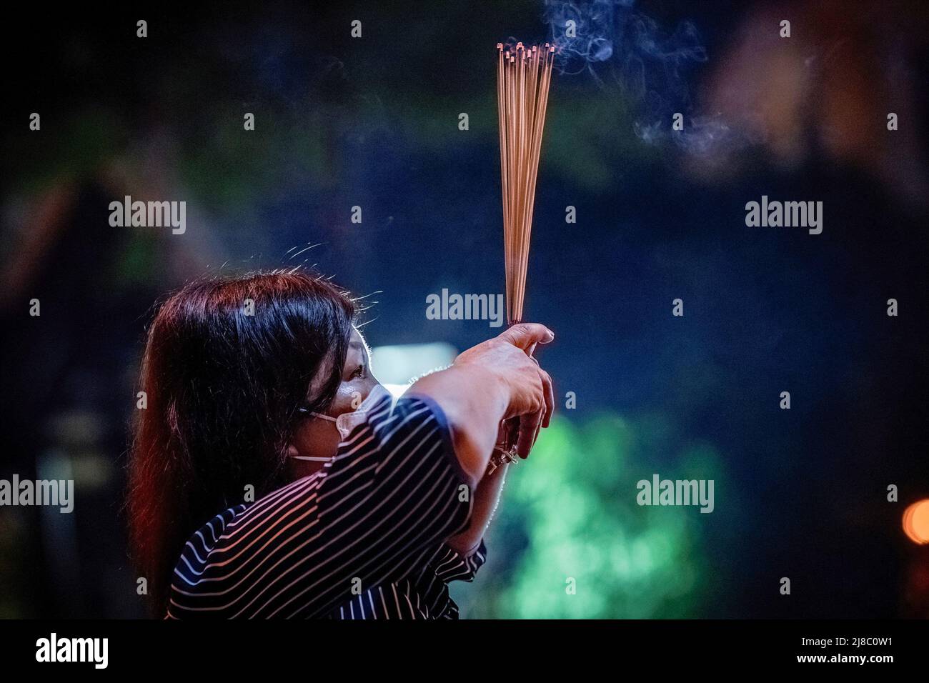 A woman holding 'joss sticks' performs a prayer ritual in conjunction ...