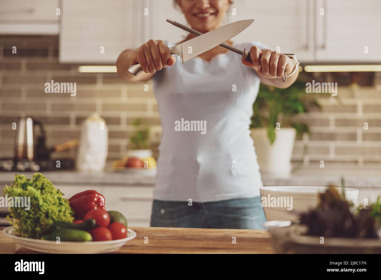 A housewife sharpens a knife standing at a table against the background ...