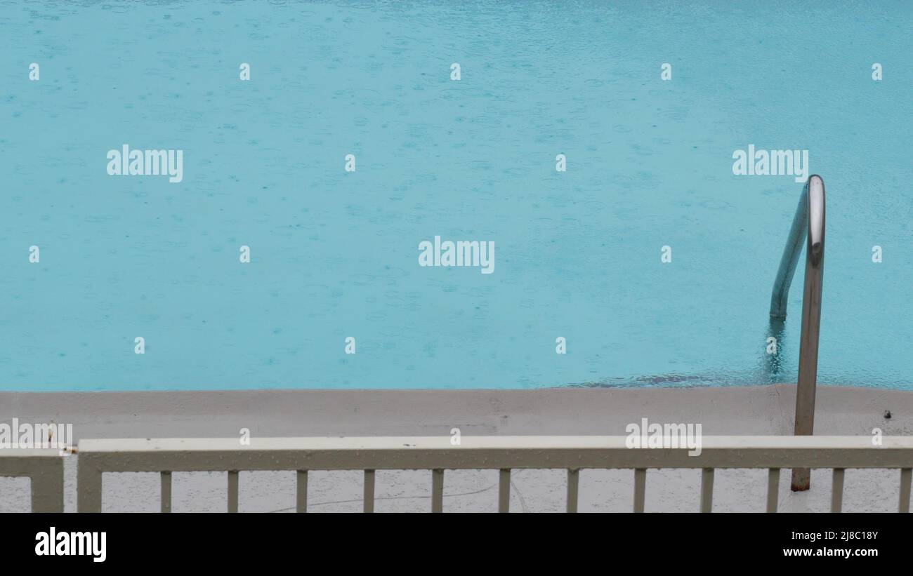 Rain drops falling on water surface of blue swimming pool, rainy day in ...