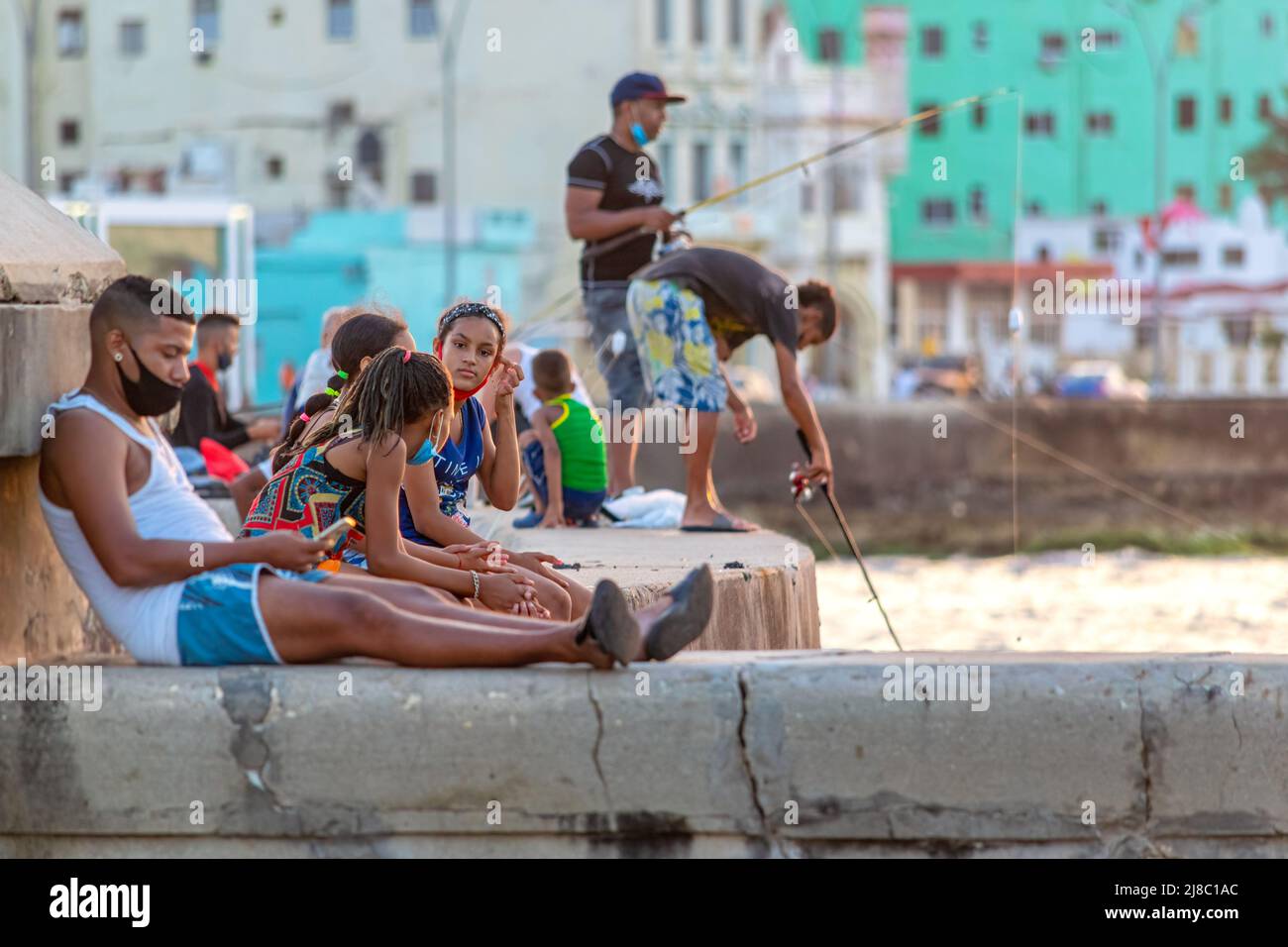 Young Cuban people sits in El Malecon retaining wall or seawall. Other ...