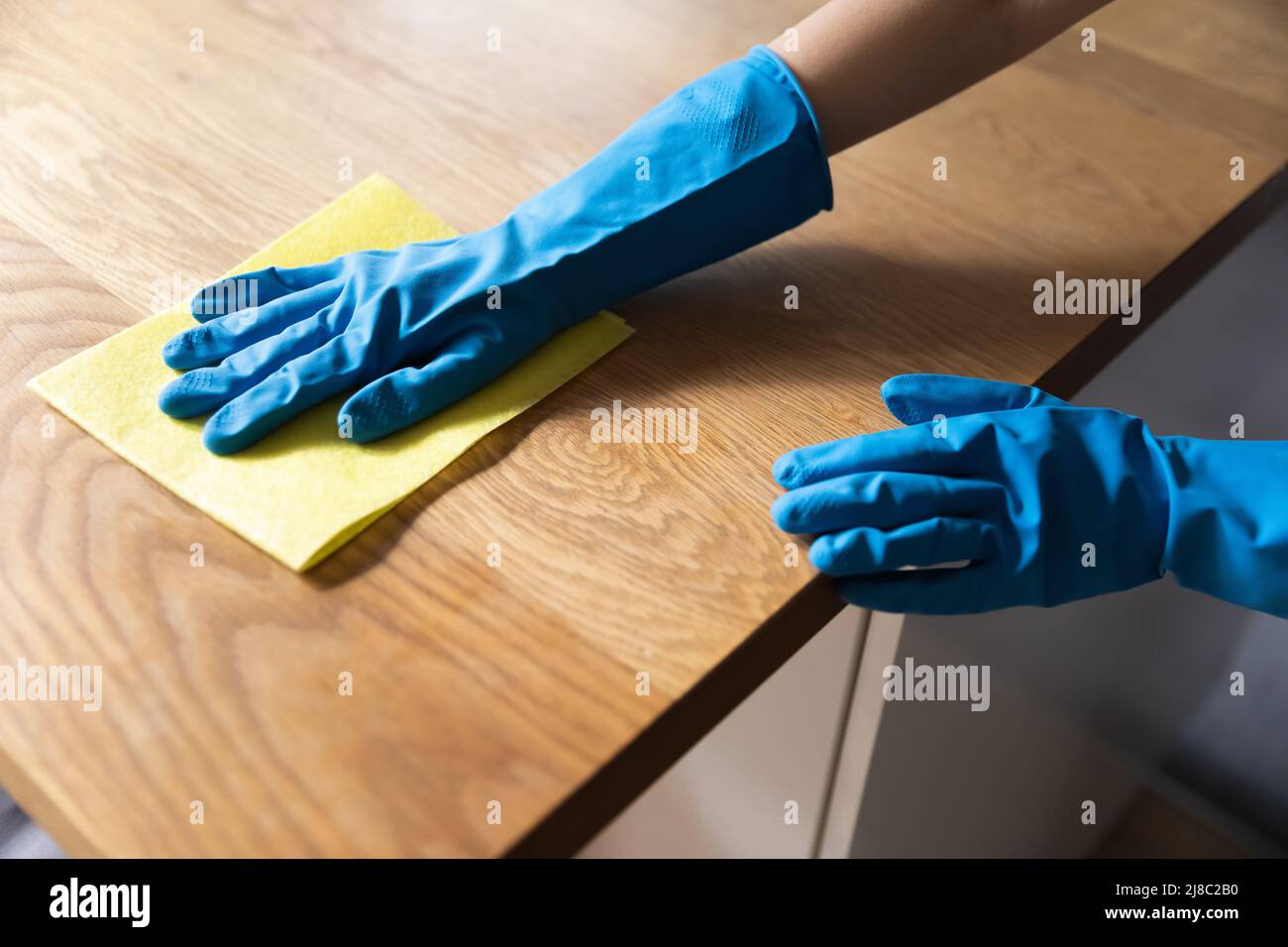 Hand of cleaner wearing blue protective rubber gloves, washing tabletop ...